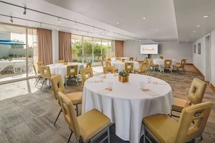 Sala de conferências com mesas redondas, cadeiras e uma tela grande.