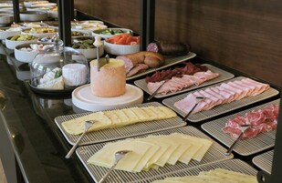 Um buffet com diversos queijos, carnes e legumes.