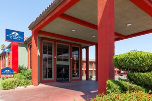 Entrada de hotel com fachada vermelha e verde, grandes portas de vidro e área externa coberta.