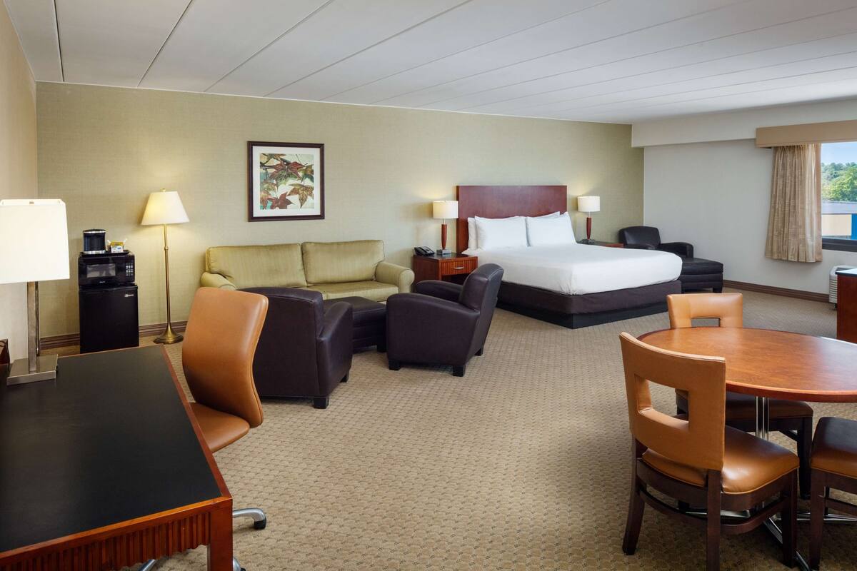 Quarto de hotel com cama, sofá, escrivaninha e mesa de jantar.