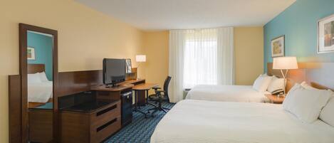 Quarto de hotel com duas camas, uma mesa de trabalho com televisão, espelho e janela com cortinas.