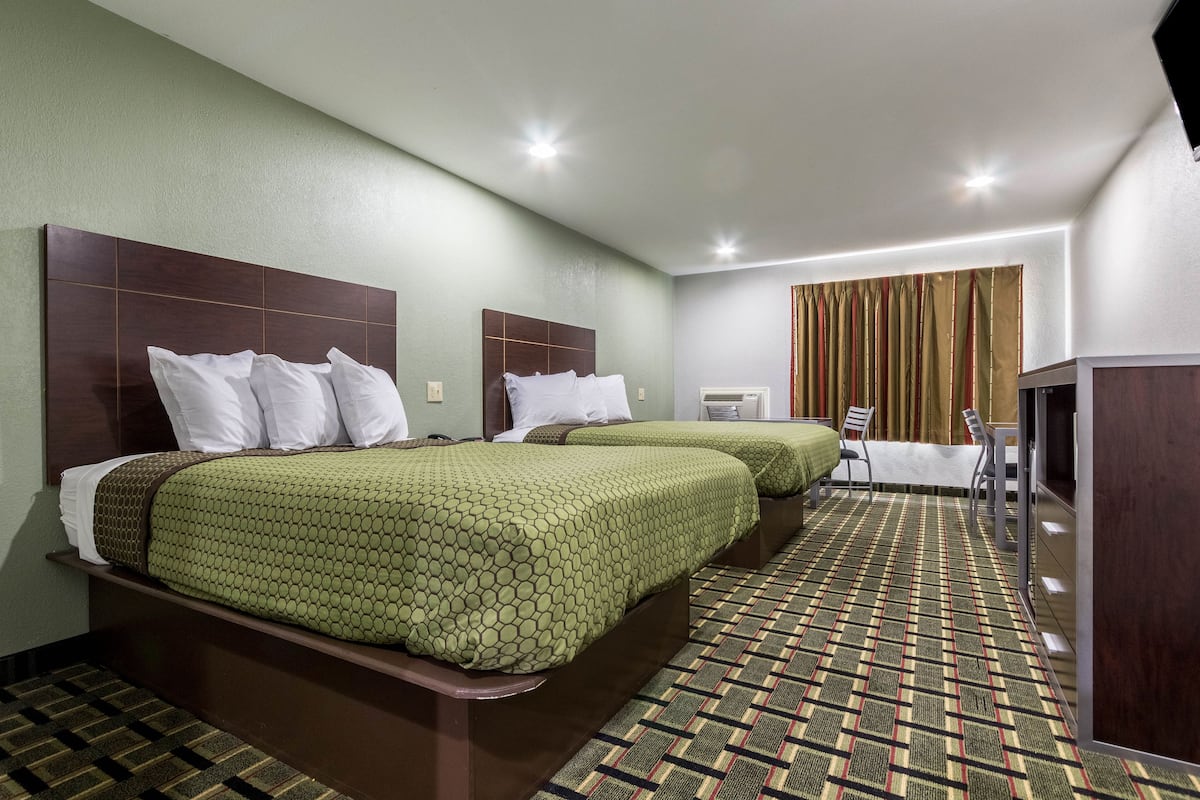 Quarto de hotel com duas camas, televisão de tela plana, escrivaninha e janela com cortinas.