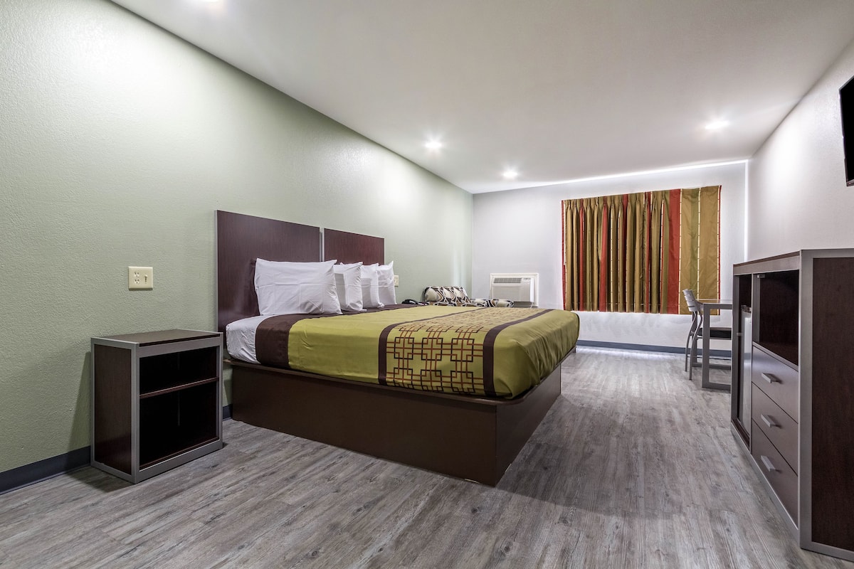 Quarto de hotel com cama, mesa de cabeceira, guarda-roupa e janela com cortinas.