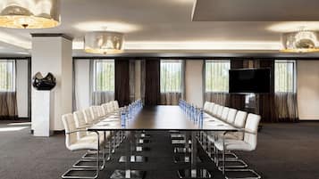 Uma sala de conferências com uma mesa comprida, cadeiras brancas e uma tela de televisão.