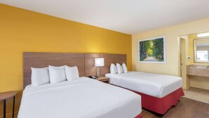 Quarto de hotel com duas camas, uma cabeceira de madeira, uma mesa de cabeceira com abajur e um quadro na parede.