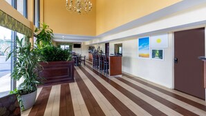Um hall de hotel com um balcão de recepção longo, plantas em vasos e obras de arte nas paredes.