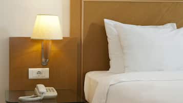Quarto de hotel com mesa de cabeceira, luminária, telefone e cama com roupa de cama branca.