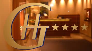 Uma área de recepção de hotel com um grande logotipo exibindo um 'H' estilizado e quatro estrelas.