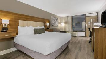 Quarto de hotel com uma cama grande, mesas de cabeceira com luminárias, uma escrivaninha com cadeira e uma televisão.