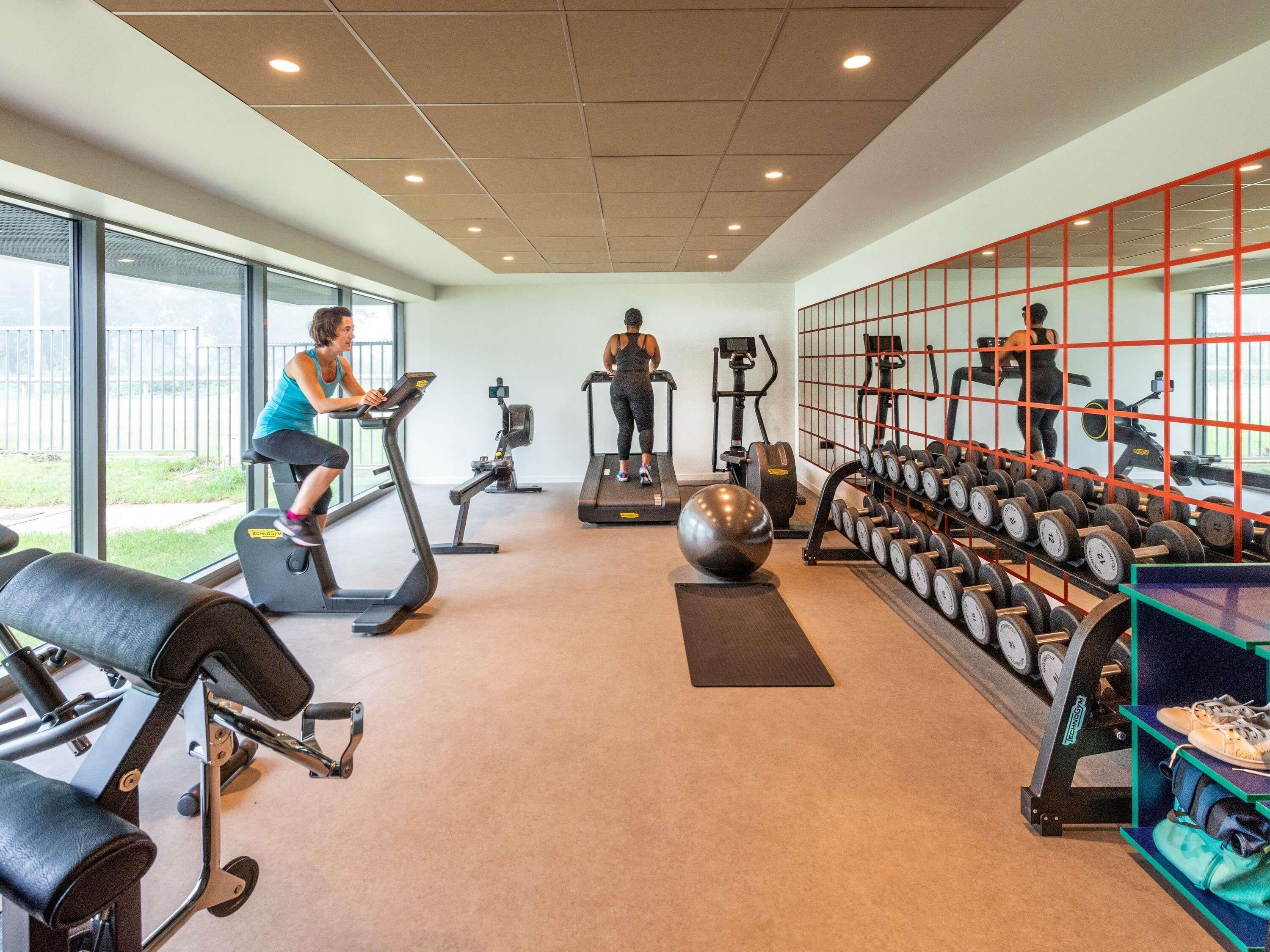Uma academia com esteiras, bolas de exercício e halteres.
