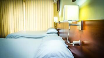 Quarto de hotel com cama, mesa de cabeceira, abajur e janela com persianas.