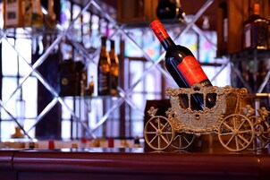 Uma garrafa de vinho em um carrinho decorativo sobre um balcão de bar.