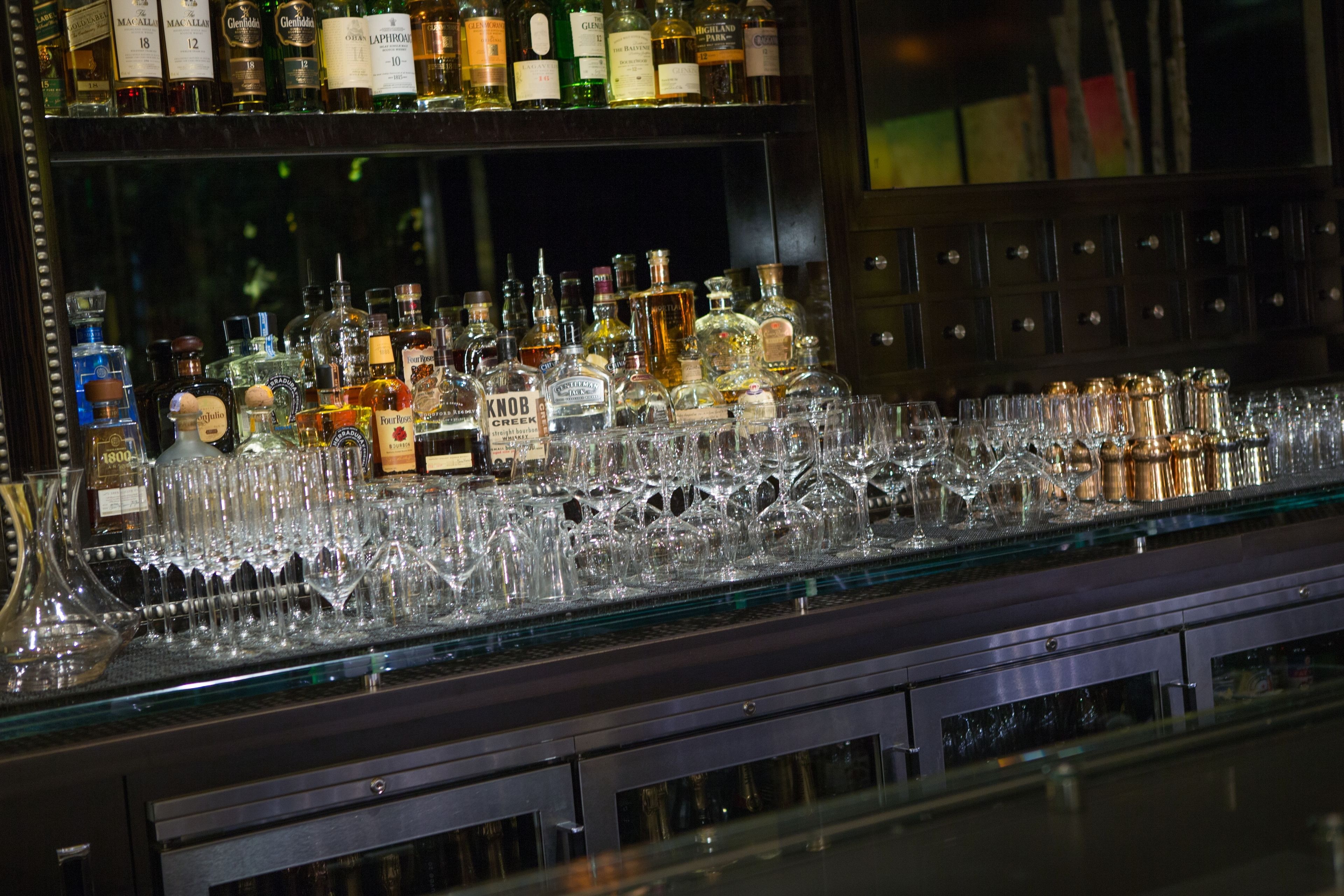 Um balcão de bar com várias garrafas de bebidas e muitos copos.