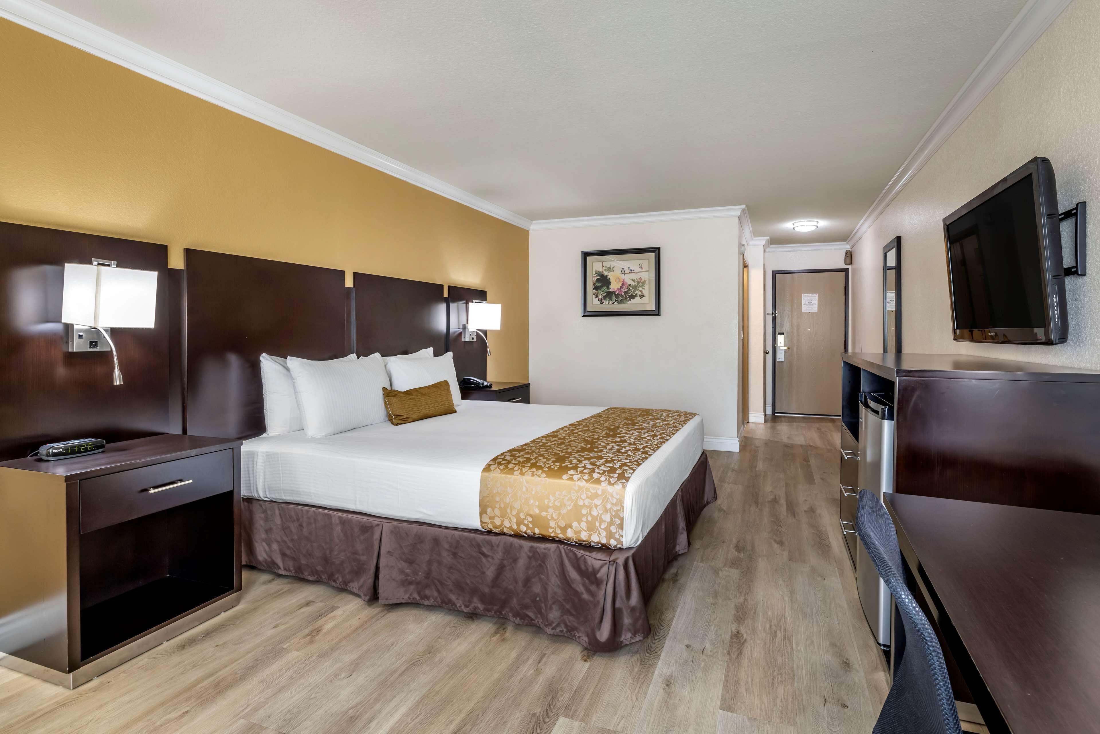 Quarto de hotel com cama grande, mesas de cabeceira, escrivaninha e televisão.