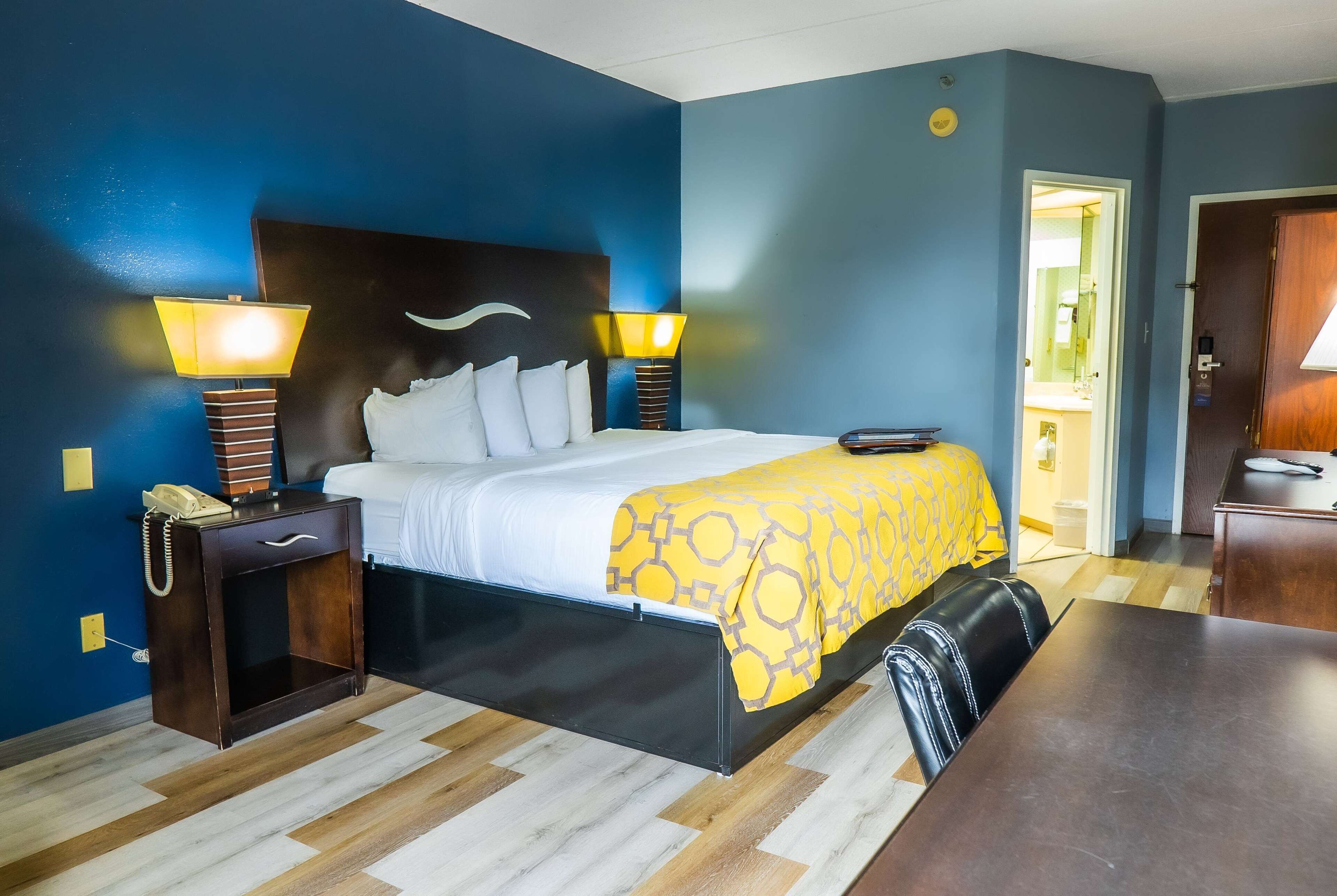 Quarto de hotel com cama, luminárias de cabeceira, mesa de apoio com telefone e piso de madeira.