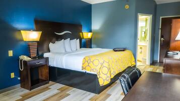 Quarto de hotel com cama, luminárias de cabeceira, mesa de apoio com telefone e piso de madeira.