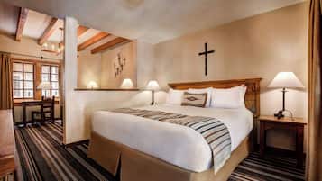 Quarto de hotel bem arrumado com uma cama grande, abajures, cabeceira de madeira, uma cruz na parede e uma janela com cortinas.
