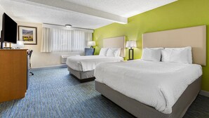 Quarto de hotel com duas camas, uma escrivaninha, uma televisão e uma janela com cortinas.