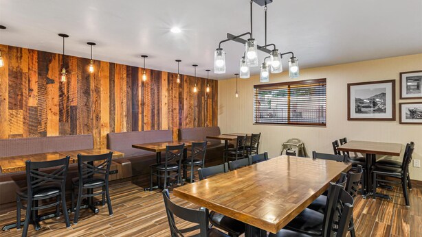 Um restaurante com painéis de madeira, diversas opções de assento incluindo cabines e mesas, e iluminação pendente.