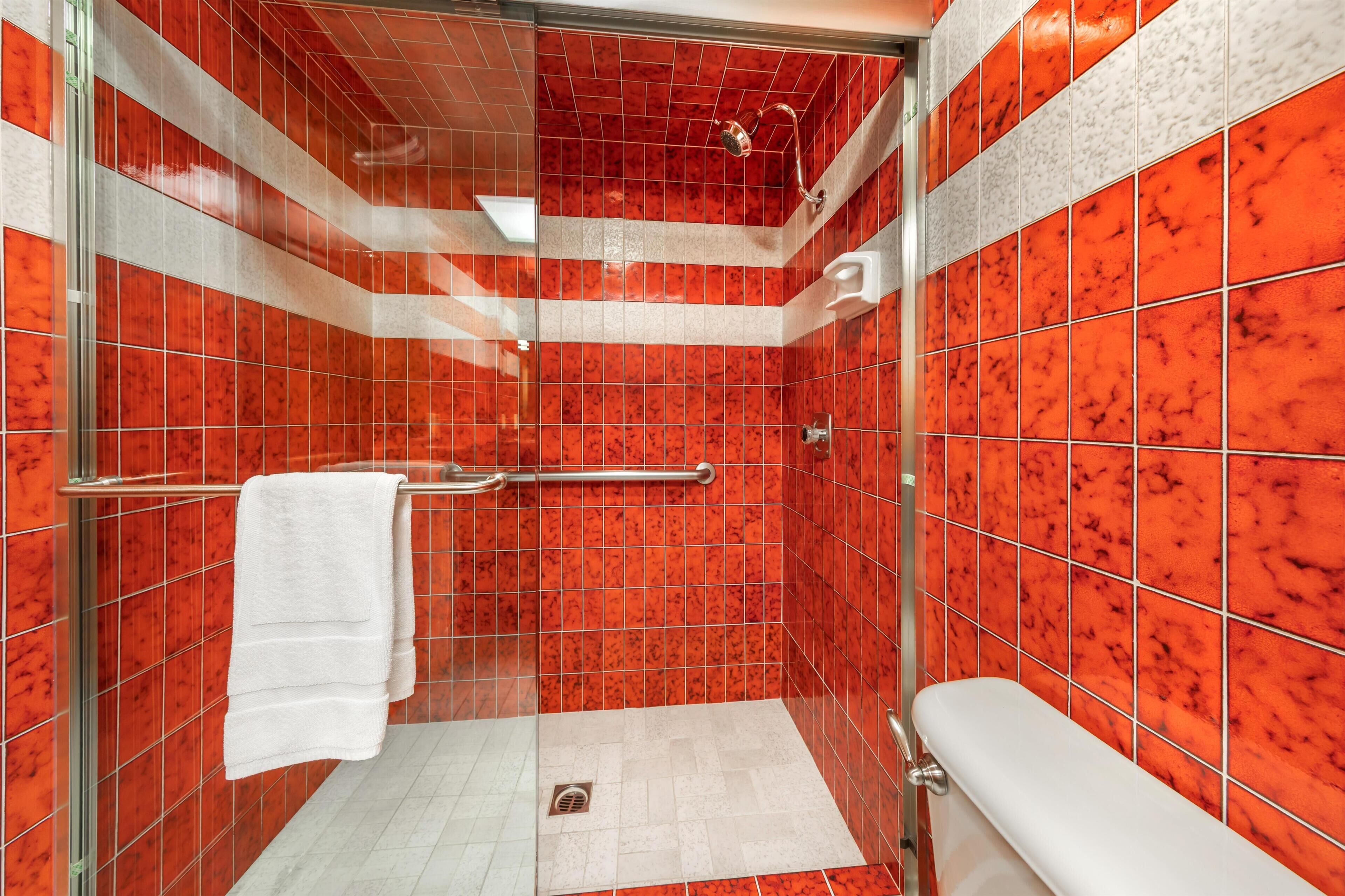 Casa de banho com azulejos vermelhos e brancos, cabine de duche em vidro, banheira branca e um porta-toalhas.