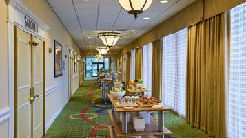 Um corredor de hotel com carpete estampado em verde, uma mesa de buffet com comida e uma placa com o dizer 'SALON B'.