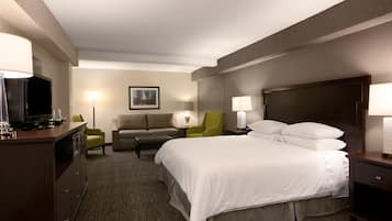 Quarto de hotel com uma cama grande, uma escrivaninha com televisão de tela plana, um sofá e duas cadeiras.