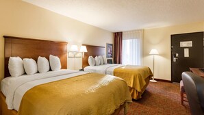 Quarto de hotel com duas camas, uma escrivaninha, uma cadeira, um abajur e uma porta com um aviso.