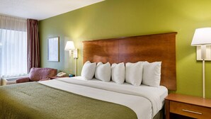 Quarto de hotel com cama, abajures, mesa de cabeceira, cadeira e janela com cortinas.
