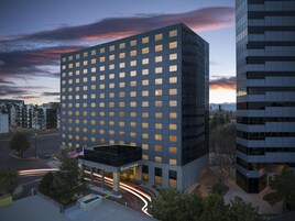 Um hotel moderno com uma grade de janelas, uma bandeira americana visível e vista da área urbana ao redor.