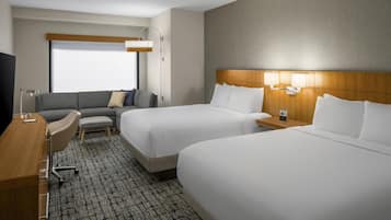 Quarto de hotel com duas camas, uma escrivaninha, um sofá e uma televisão.