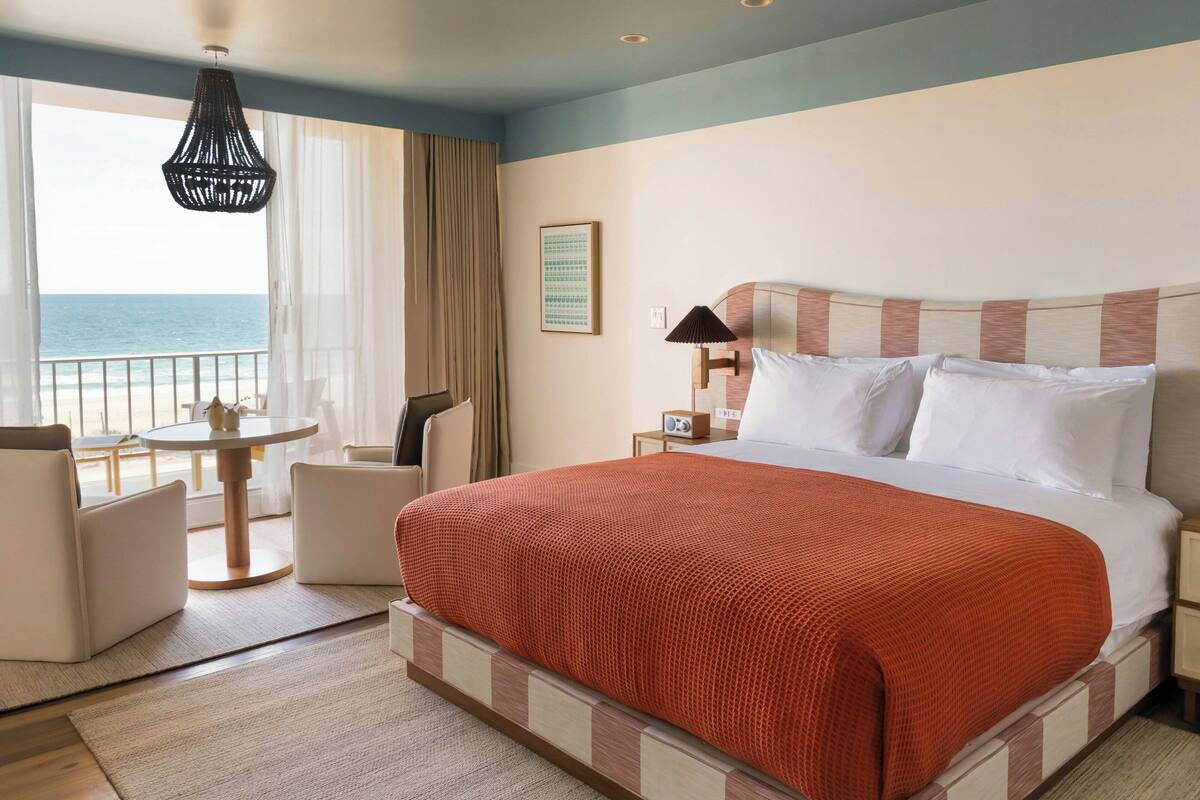 Quarto de hotel com uma cama grande, vista para o oceano, uma mesa redonda e duas cadeiras.