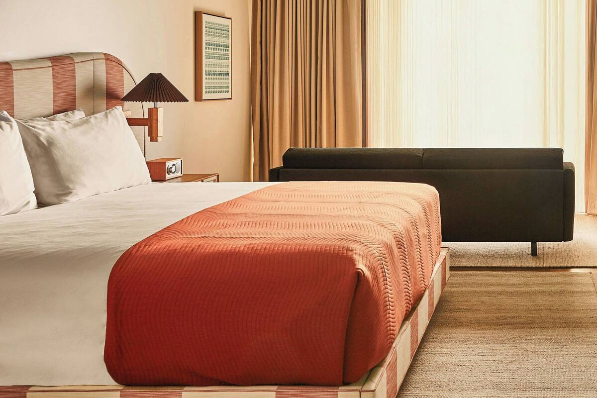 Quarto de hotel com uma cama grande, um sofá, uma mesa de cabeceira com abajur e um quadro na parede.