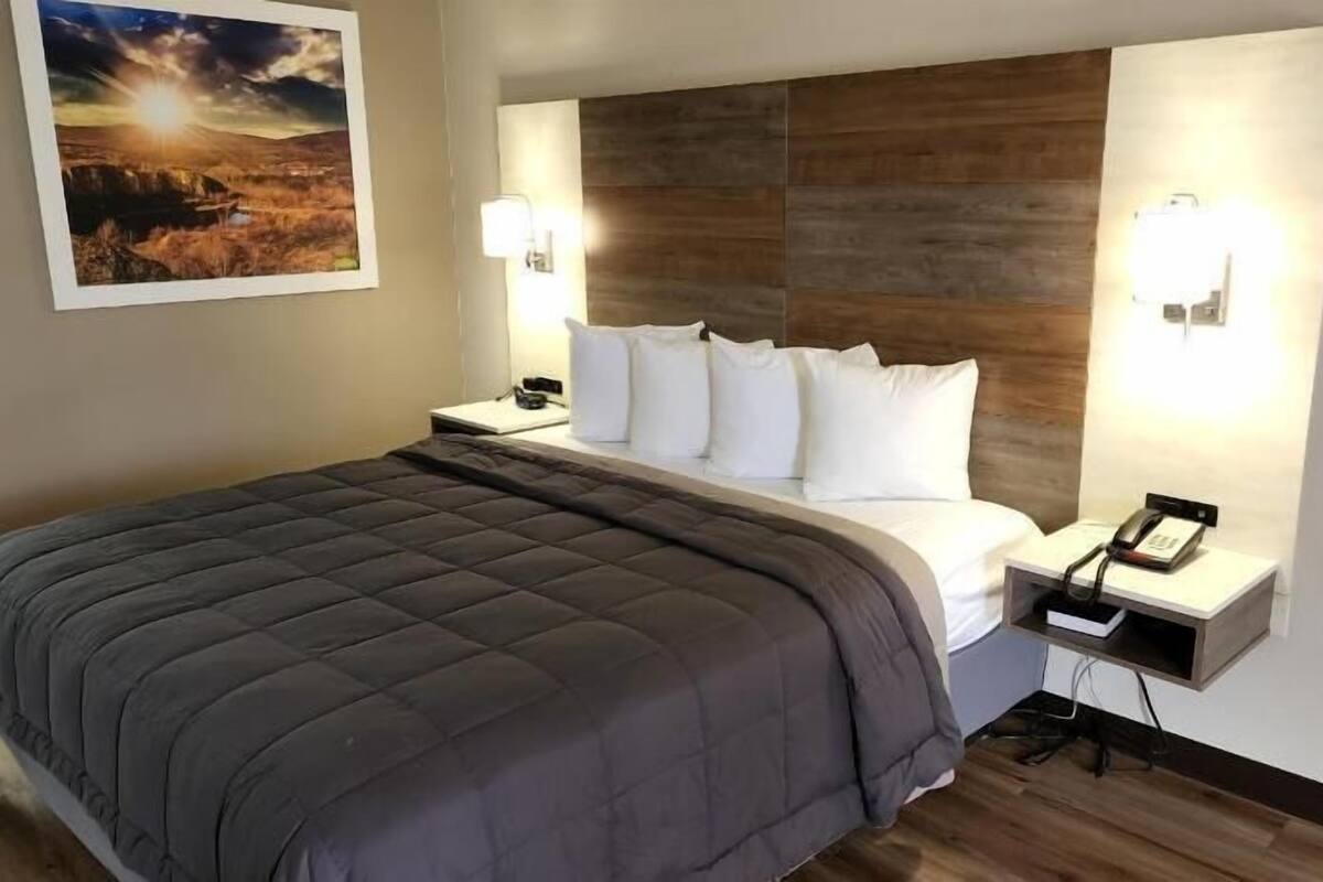 Quarto de hotel com cama, luminárias de cabeceira, mesa de apoio, telefone e um quadro na parede.