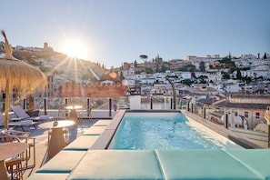 Uma piscina no terraço com espreguiçadeiras e uma mesa, com vista para uma cidade situada numa colina.