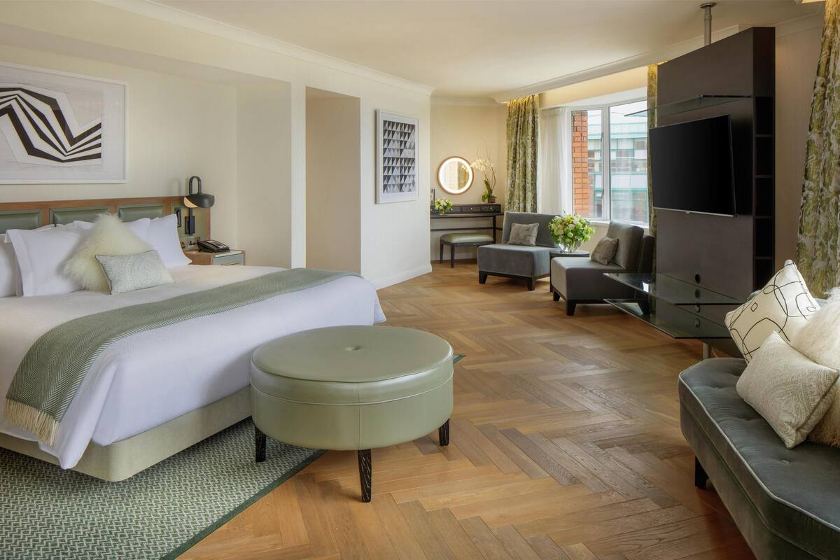 Quarto de hotel com uma cama grande, um sofá, uma televisão e uma escrivaninha com uma cadeira.