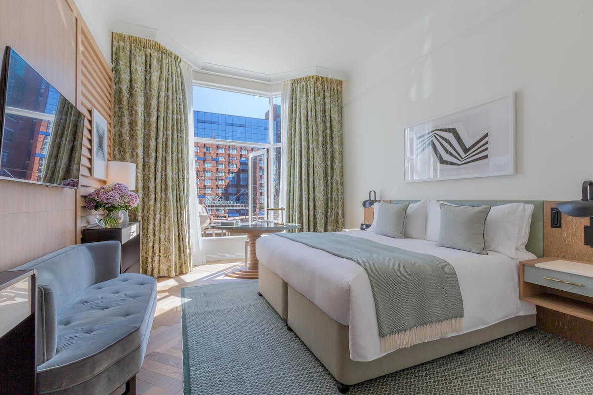 Quarto de hotel com uma cama grande, um sofá, uma televisão e varanda com cortinas.