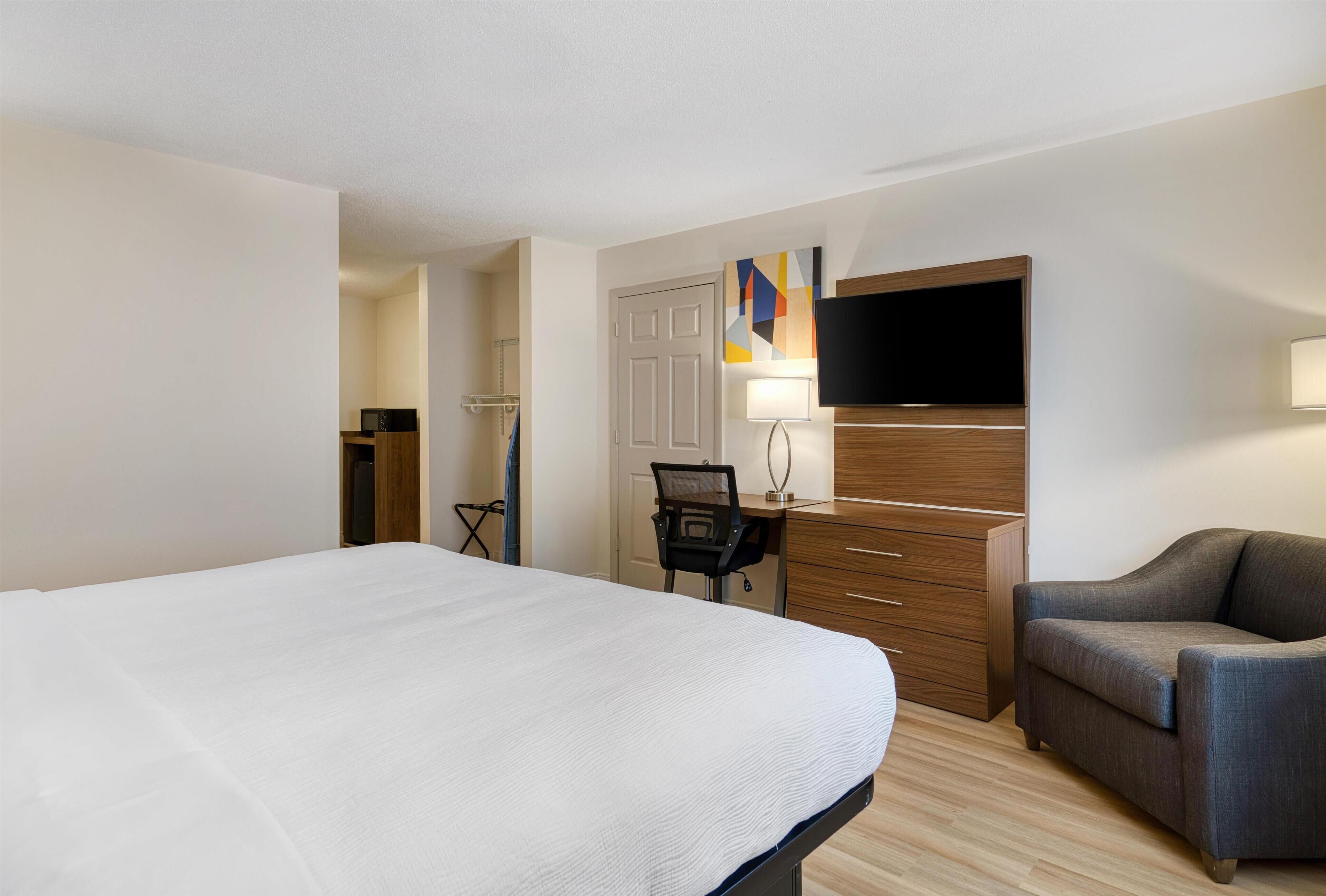 Quarto de hotel com uma cama grande, uma escrivaninha com cadeira, televisão e um sofá.