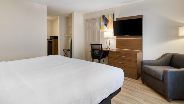 Quarto de hotel com uma cama grande, uma escrivaninha com cadeira, televisão e um sofá.