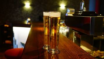 Duas cervejas em copos altos sobre um balcão de madeira, com fundo escuro e uma máquina de café.