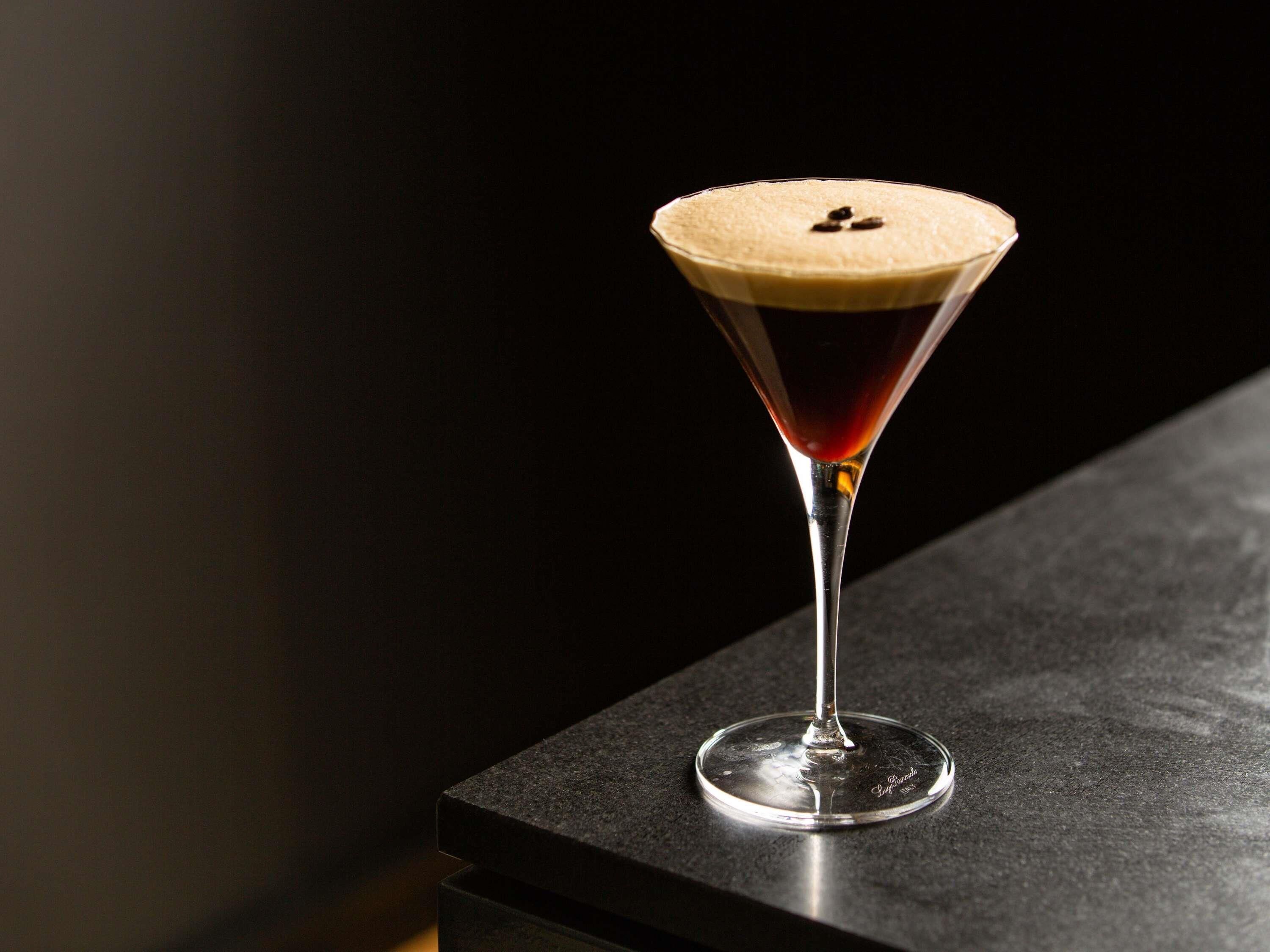 Um copo de martini com espuma cremosa sobre uma superfície escura.