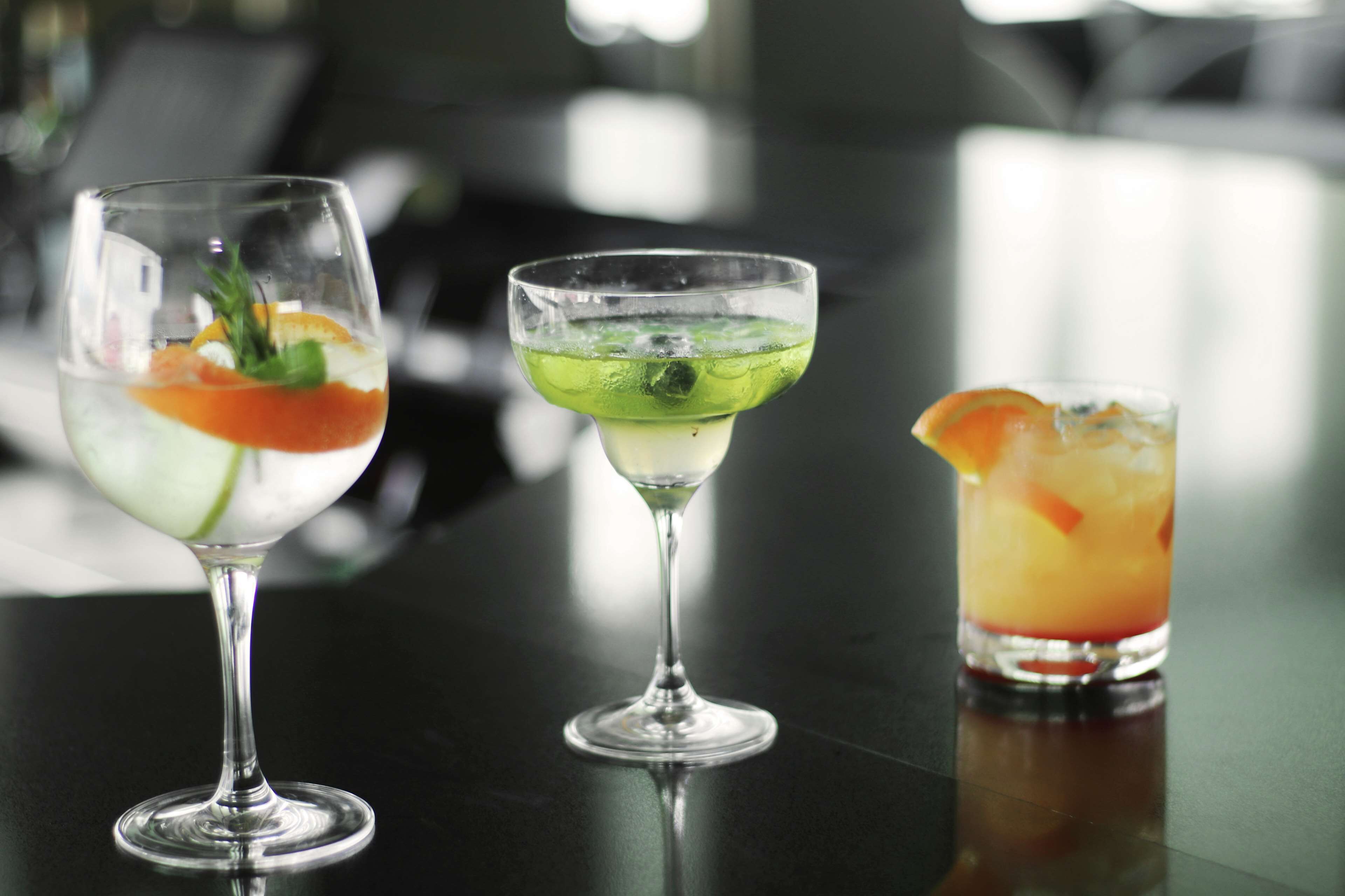 Três cocktails sobre uma superfície refletora.