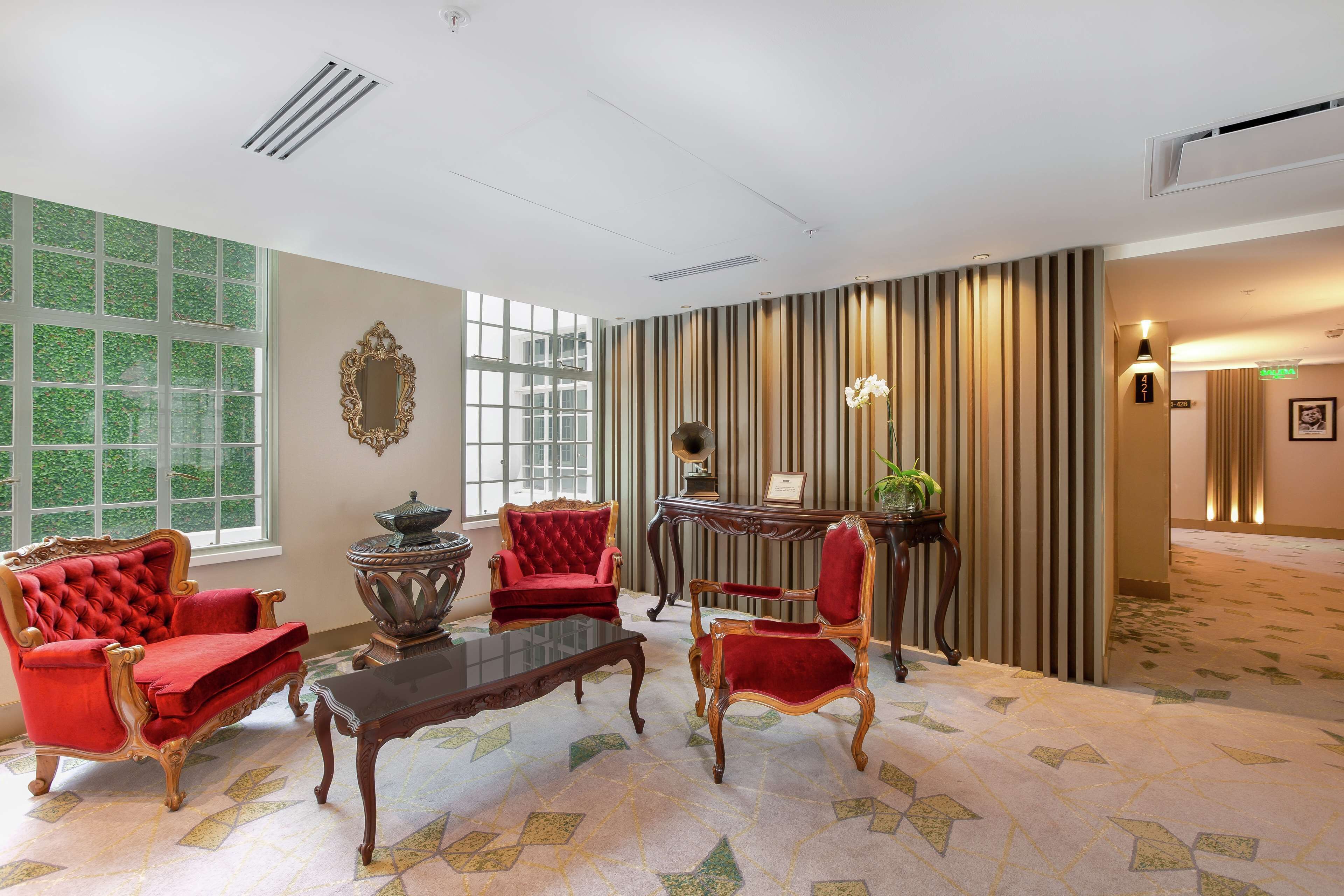 Um hall amplo com uma grande janela, confortáveis poltronas vermelhas revestidas, uma mesa de centro de madeira clássica e um espelho decorativo.