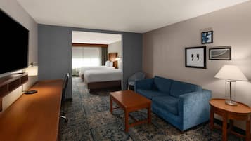 Quarto de hotel com cama, sofá azul, escrivaninha de madeira, televisão e tapete estampado.