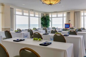 Uma sala de conferências com mesas preparadas para uma reunião, janelas amplas com vista para o mar e um pódio com microfone.