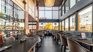 Restaurante com pé-direito alto, amplas janelas e diversas opções de assentos, incluindo mesas e cabines.
