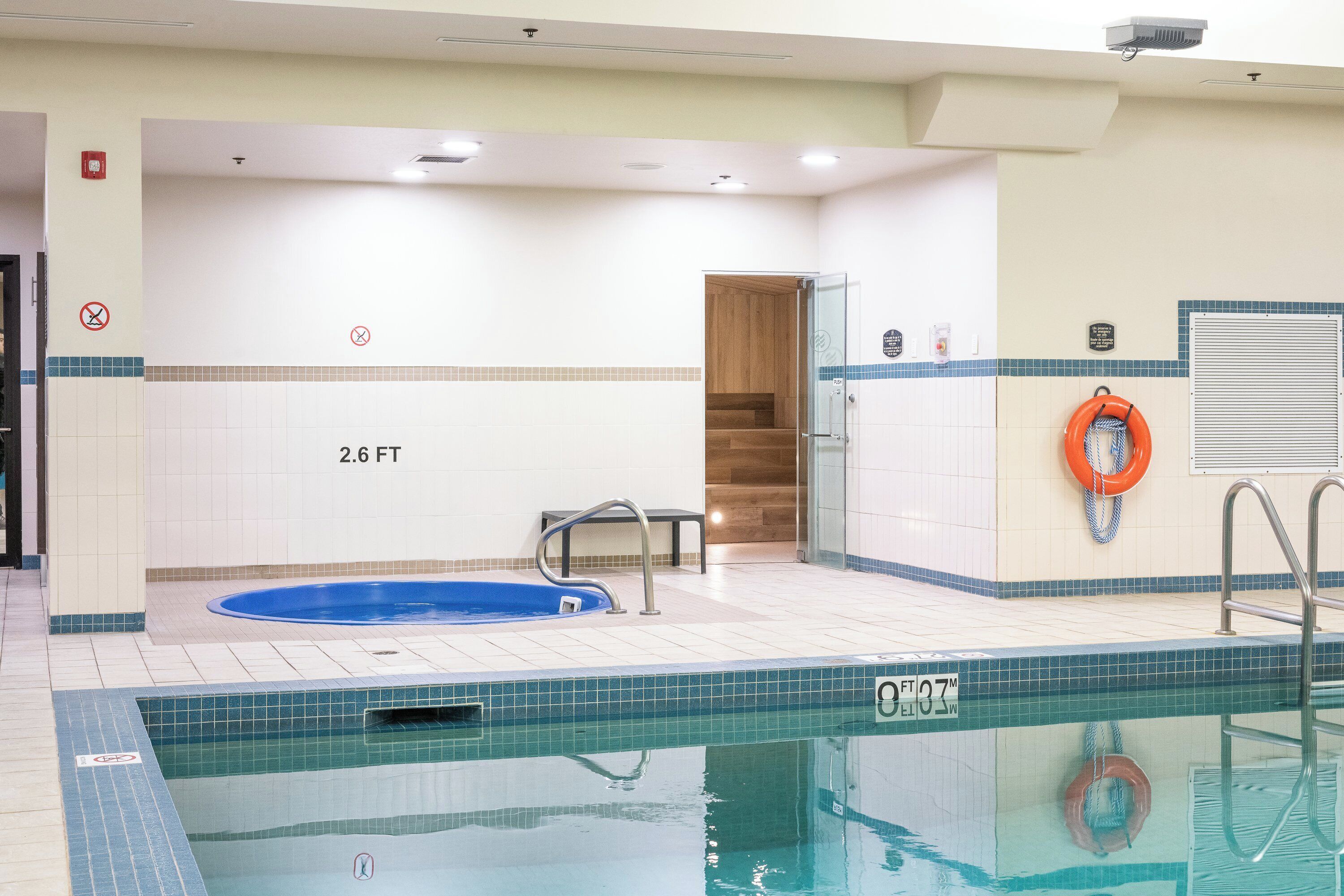 Uma piscina com indicador de profundidade, boia salva-vidas e placa de proibição de mergulho.