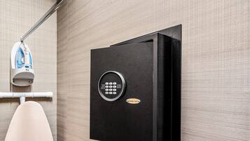 Um cofre fixado na parede com fechadura de teclado, um ferro de passar roupa pendurado e um porta-toalhas em quarto de hotel.