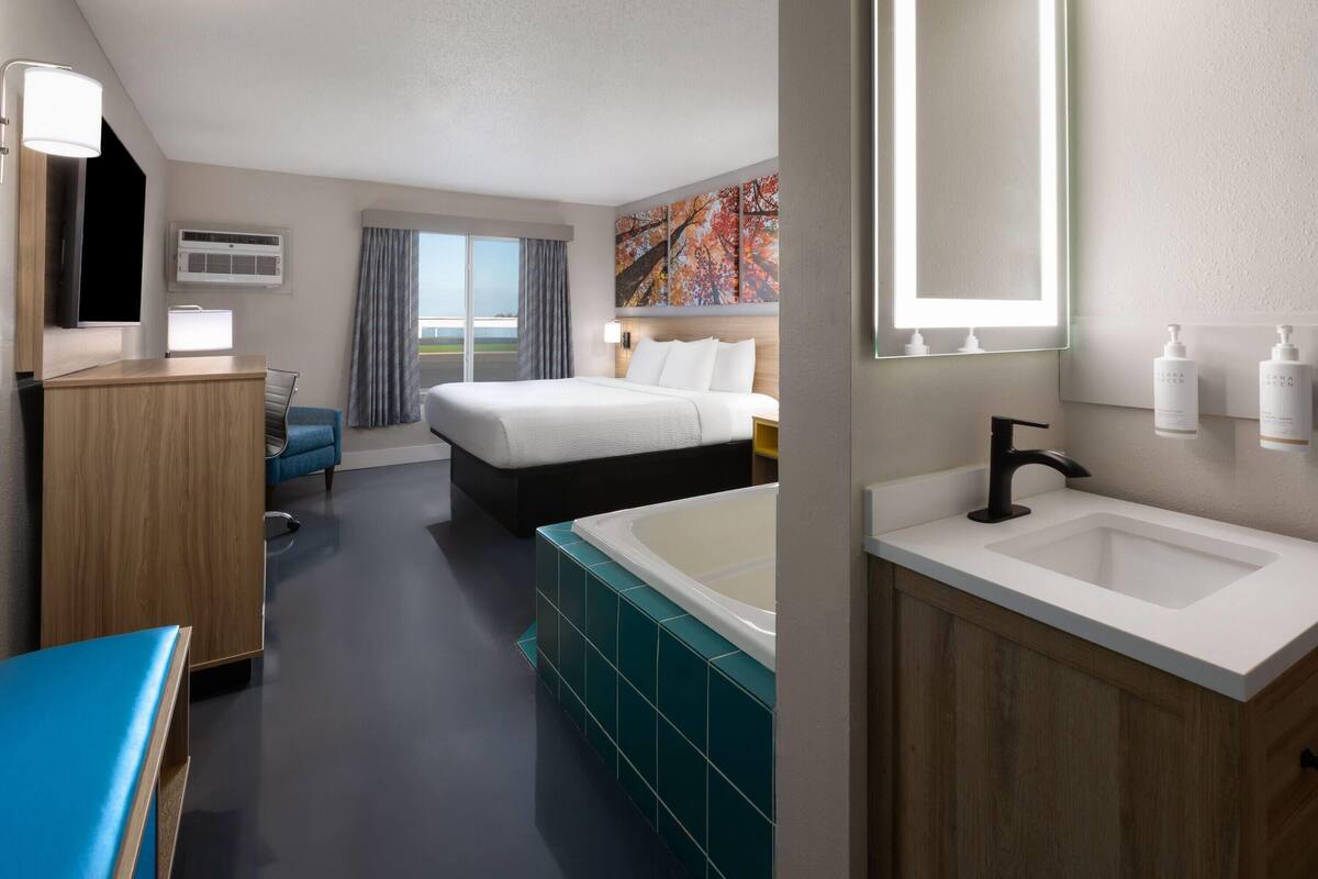 Quarto de hotel com cama, banheiro com banheira, escrivaninha, cadeira e janela com cortinas.