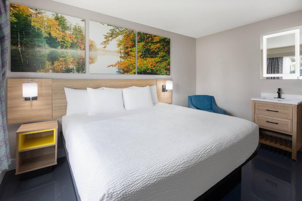 Quarto de hotel com uma cama grande, mesas de cabeceira, um espelho e uma pintura de árvores de outono.