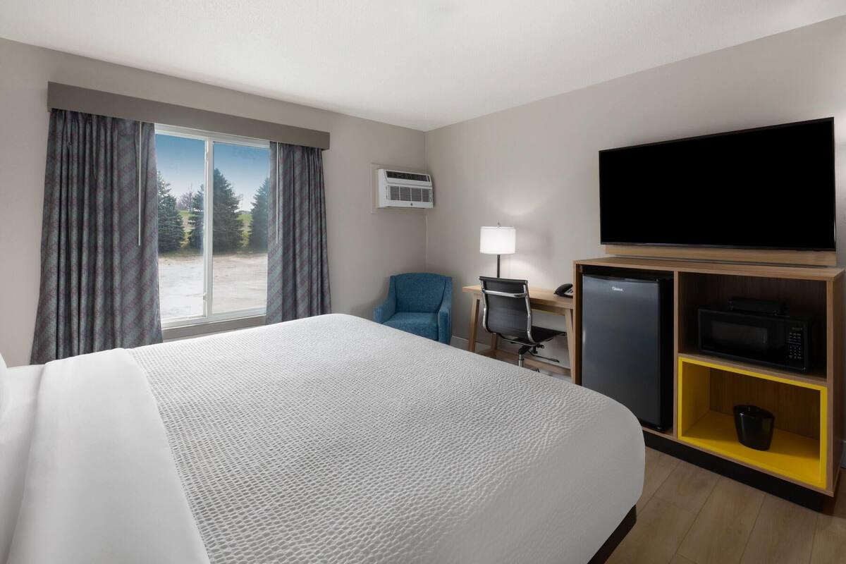 Quarto de hotel com uma cama grande, uma escrivaninha com cadeira, televisão, micro-ondas e um pequeno frigorífico.